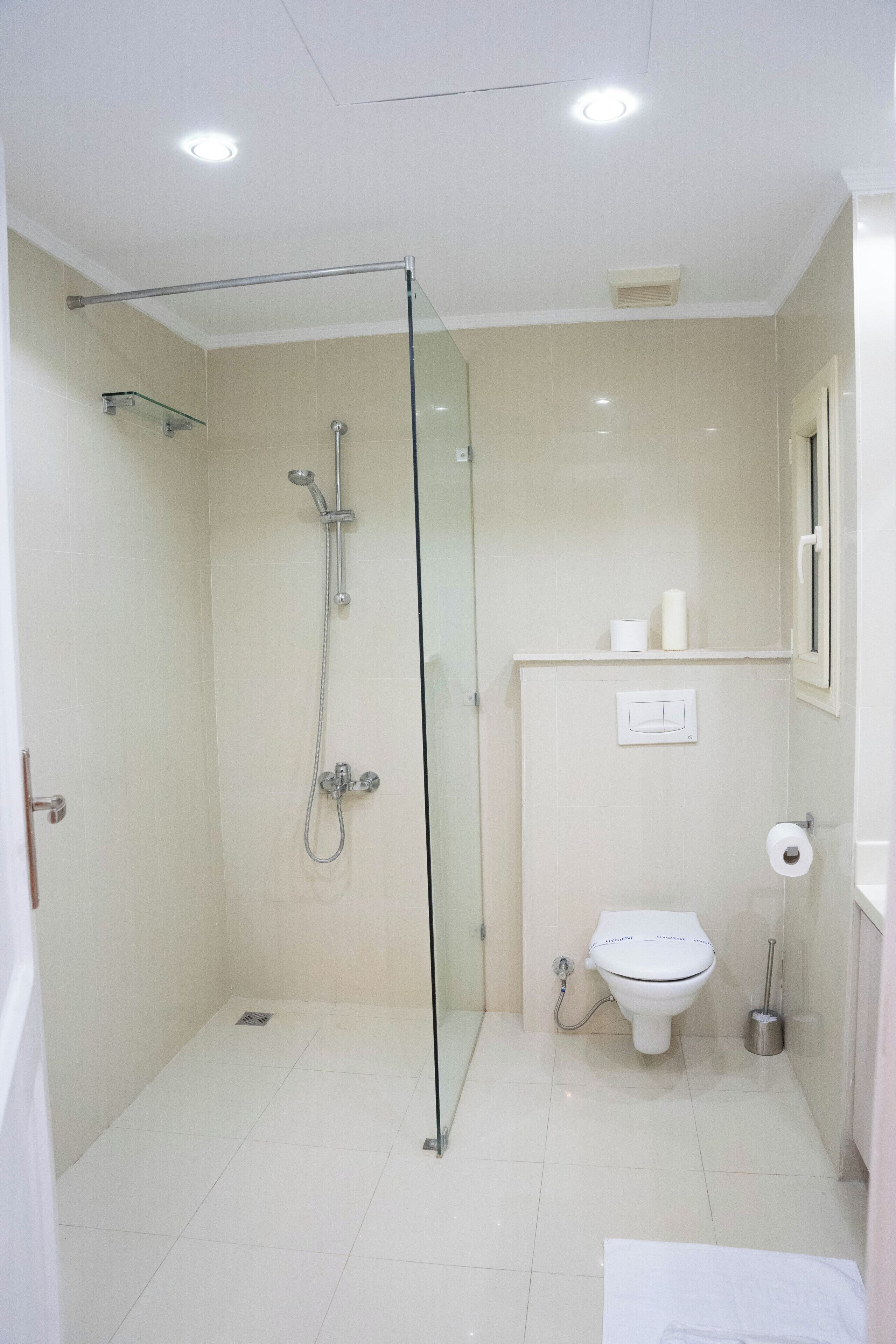 Casa de banho com chuveiro separado por vidro, sanita e lavatório.
