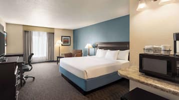Quarto de hotel com cama, escrivaninha, cadeira, luminária e micro-ondas.