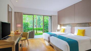 Quarto de hotel com uma cama grande, uma escrivaninha com televisão e vista para o verde lá fora.