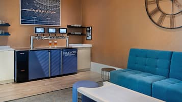 Quarto de hotel moderno com área de estar, minibar, máquina de café e um relógio de parede grande.