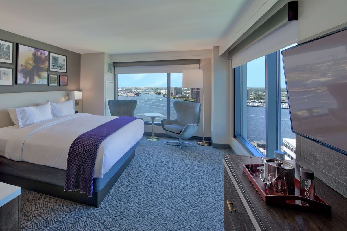 Quarto de hotel com uma cama grande, uma escrivaninha, uma cadeira, uma TV e vista para a cidade.