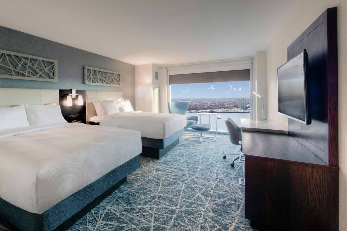 Quarto de hotel com duas camas, uma escrivaninha, televisão e vista para a cidade.