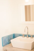 Um banheiro com pia branca, um espelho acima e parede revestida com azulejos azuis.