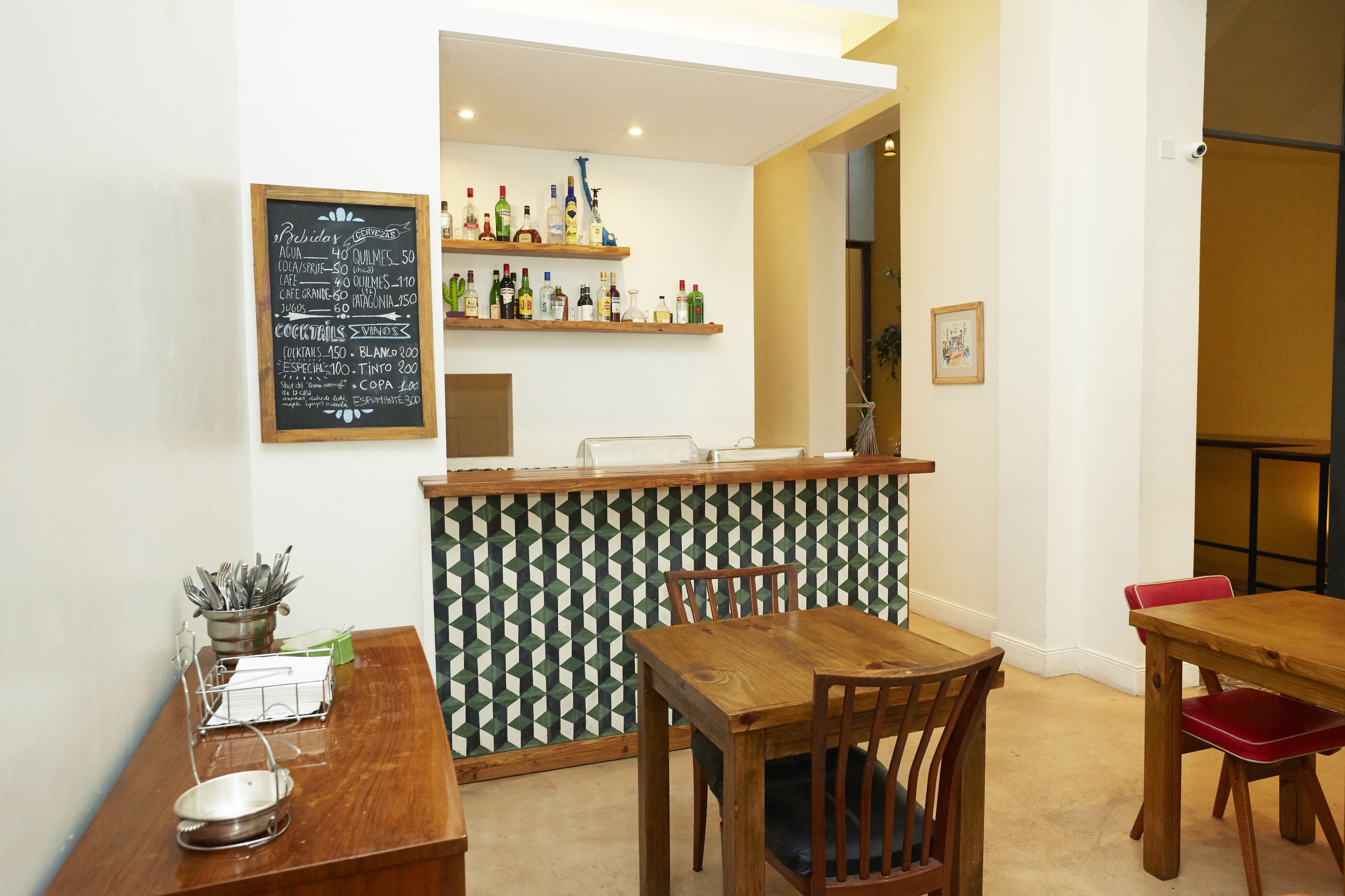 Interior de restaurante com menu em lousa, mesas de madeira, cadeiras e área de bar com prateleiras de garrafas.