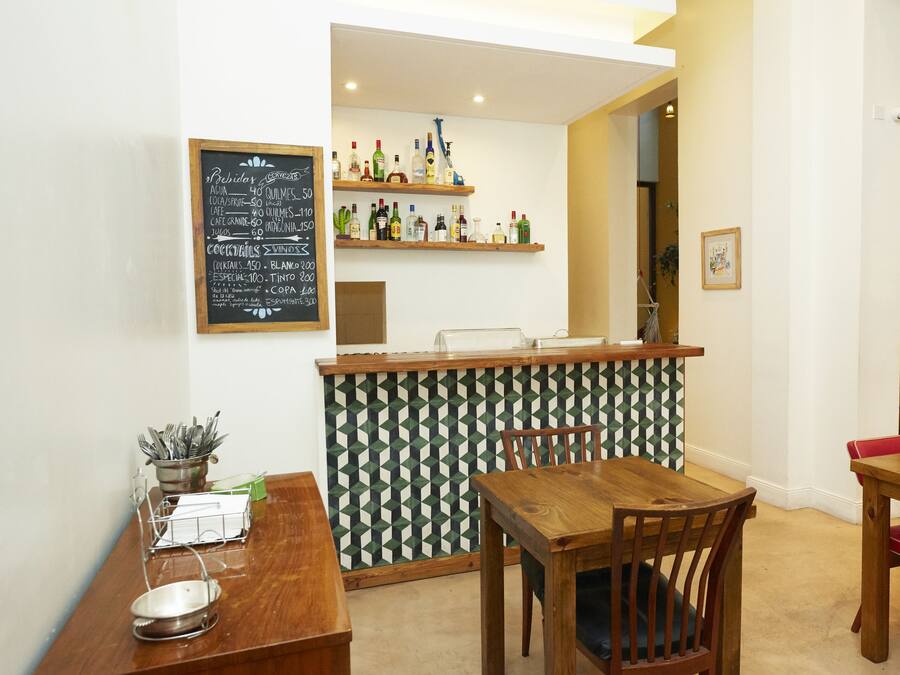 Interior de restaurante com menu em lousa, mesas de madeira, cadeiras e área de bar com prateleiras de garrafas.