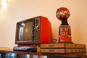 Um televisor antigo, um alto-falante vermelho e uma pilha de livros sobre uma superfície de madeira.