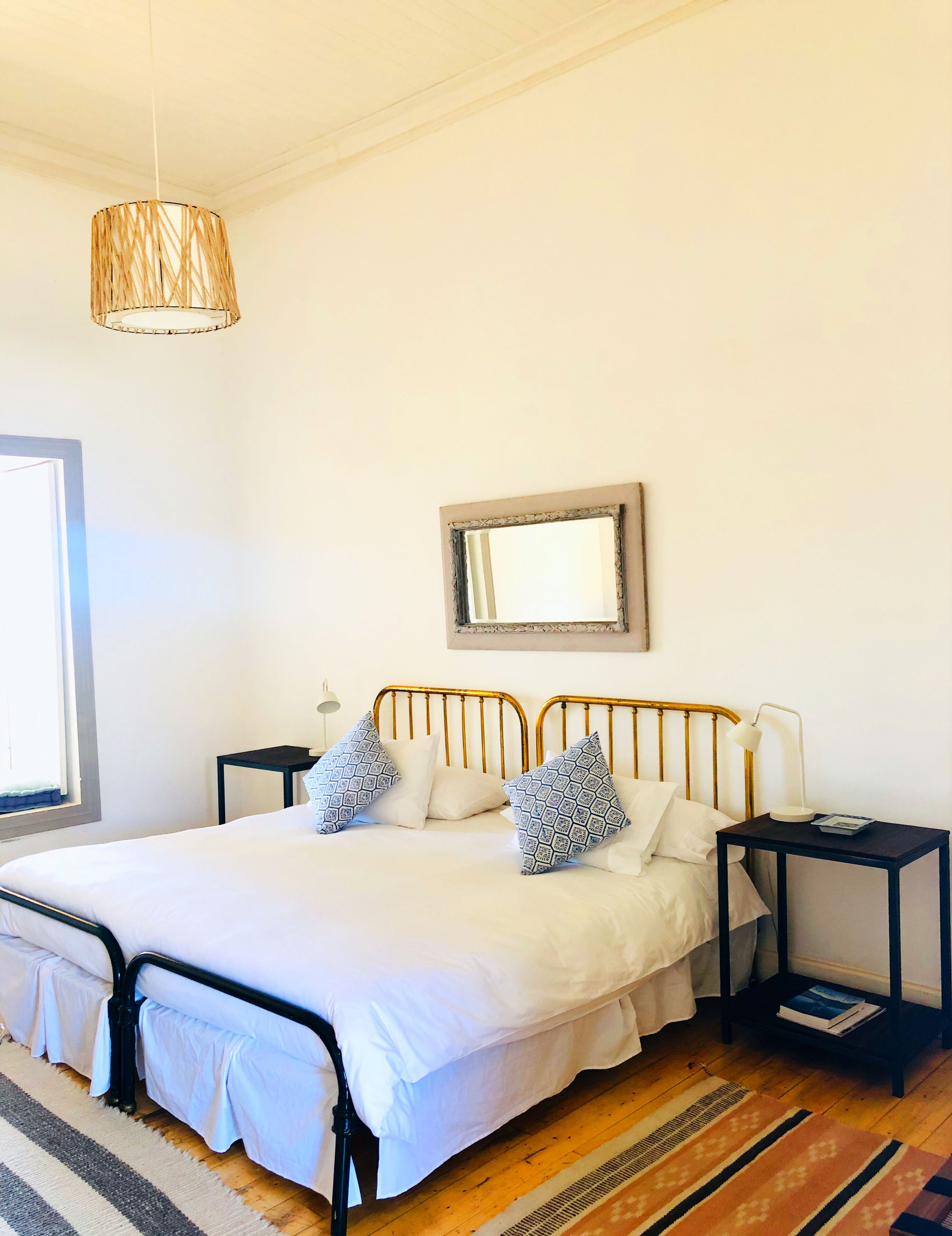 Quarto com cama, mesas de cabeceira, luminária pendente, espelho e janela.