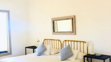 Quarto com cama, mesas de cabeceira, luminária pendente, espelho e janela.