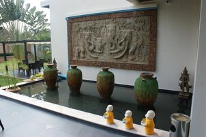 Um pátio com um elemento de água, vasos decorativos e um relevo na parede.