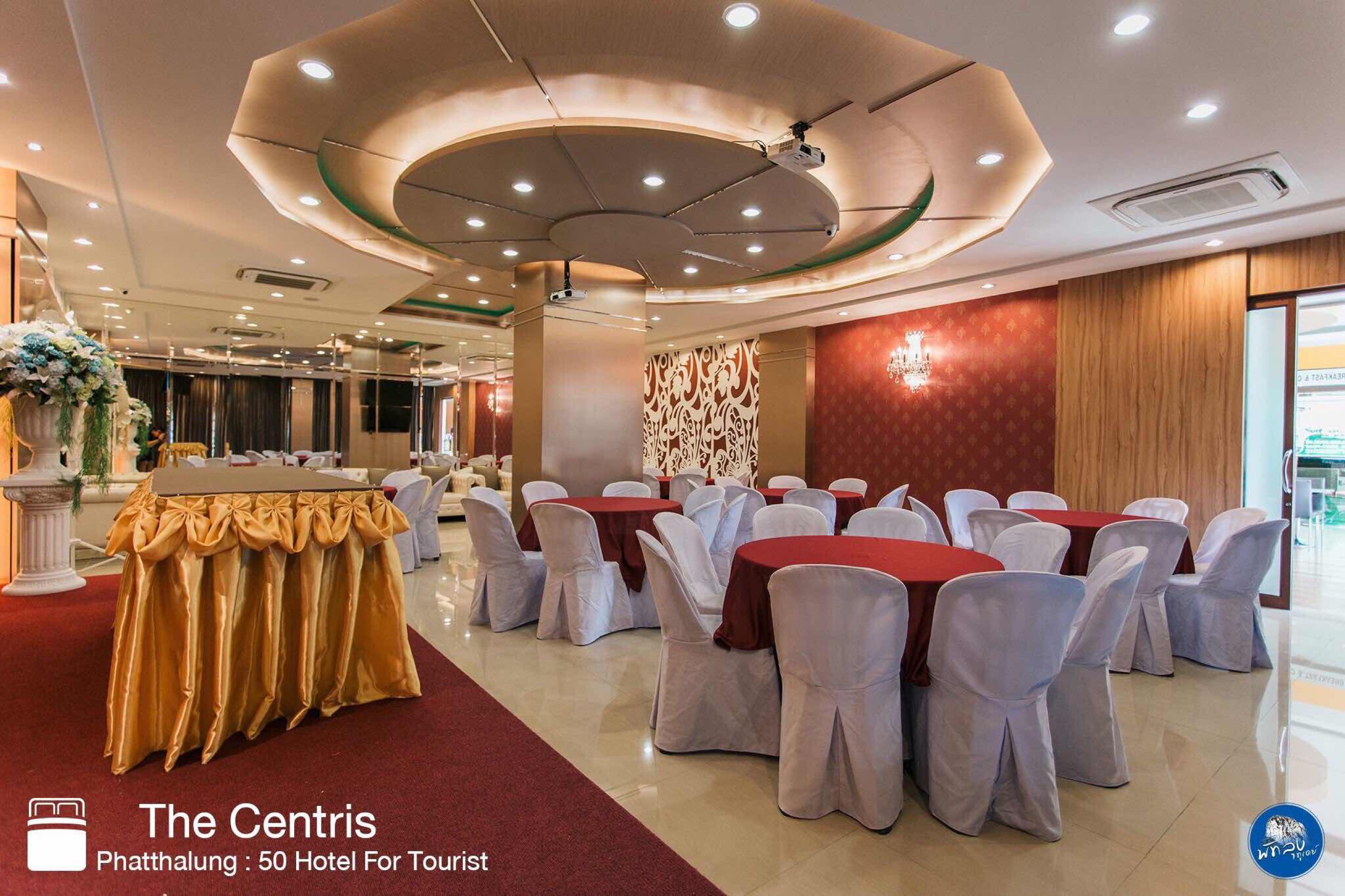 Uma sala de conferência de hotel com mesas redondas, cadeiras brancas e um tapete vermelho.