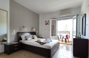 Quarto com cama, mesas de cabeceira, espelho e vista para a varanda.