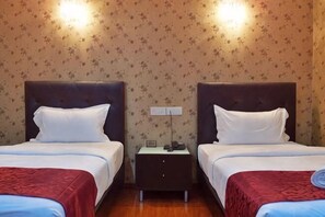 Quarto de hotel com duas camas, uma mesa de cabeceira entre elas, e uma parede com papel de parede floral.