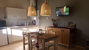 Cozinha moderna com armários brancos, uma mesa de jantar de madeira e uma TV fixada na parede.