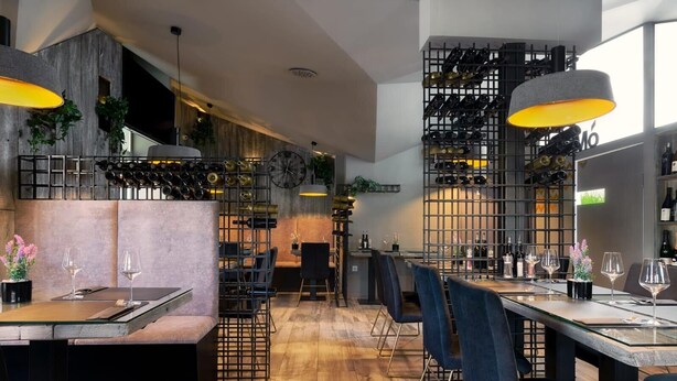 Interior moderno de restaurante com soalho de madeira, mobiliário preto e cinzento e estantes para vinho.