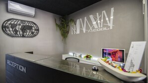 Balcão de recepção com uma placa 'RECEPTION', um mapa-múndi decorativo, uma planta e uma tela de TV exibindo um quarto.
