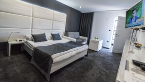 Quarto de hotel moderno com uma cama grande, mesas de cabeceira, televisão e guarda-roupa.