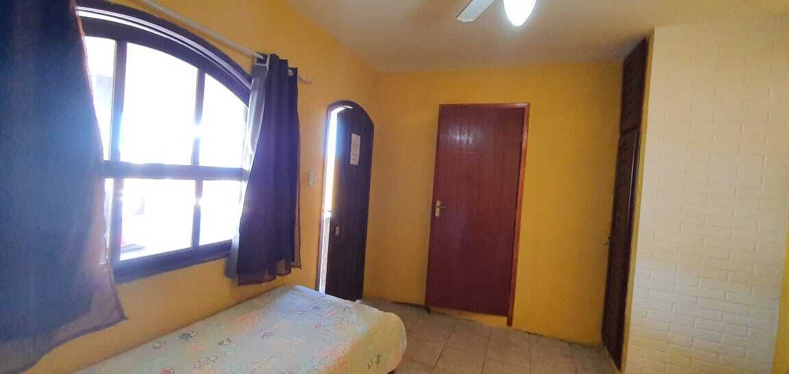 Um quarto com cama, janela com cortinas, porta e parede de tijolos brancos.