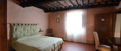 Quarto com cama, cadeira, escrivaninha e janela com cortinas.
