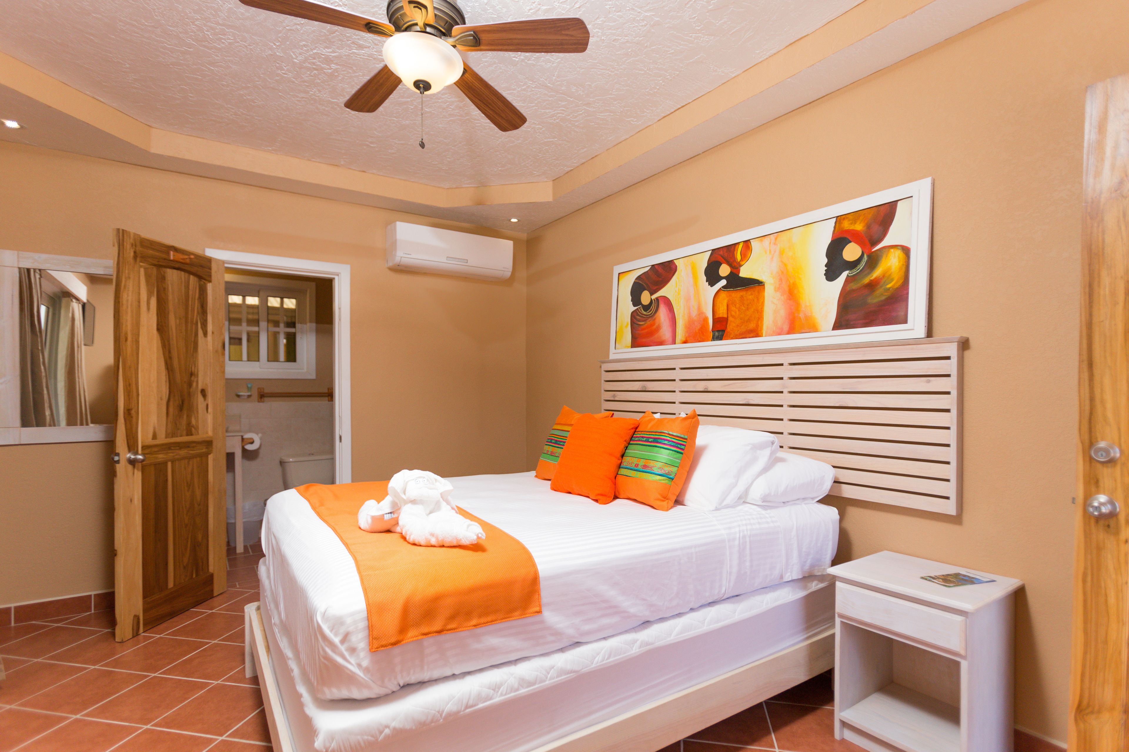 Quarto com cama, ventilador de teto, quadro e porta de madeira.