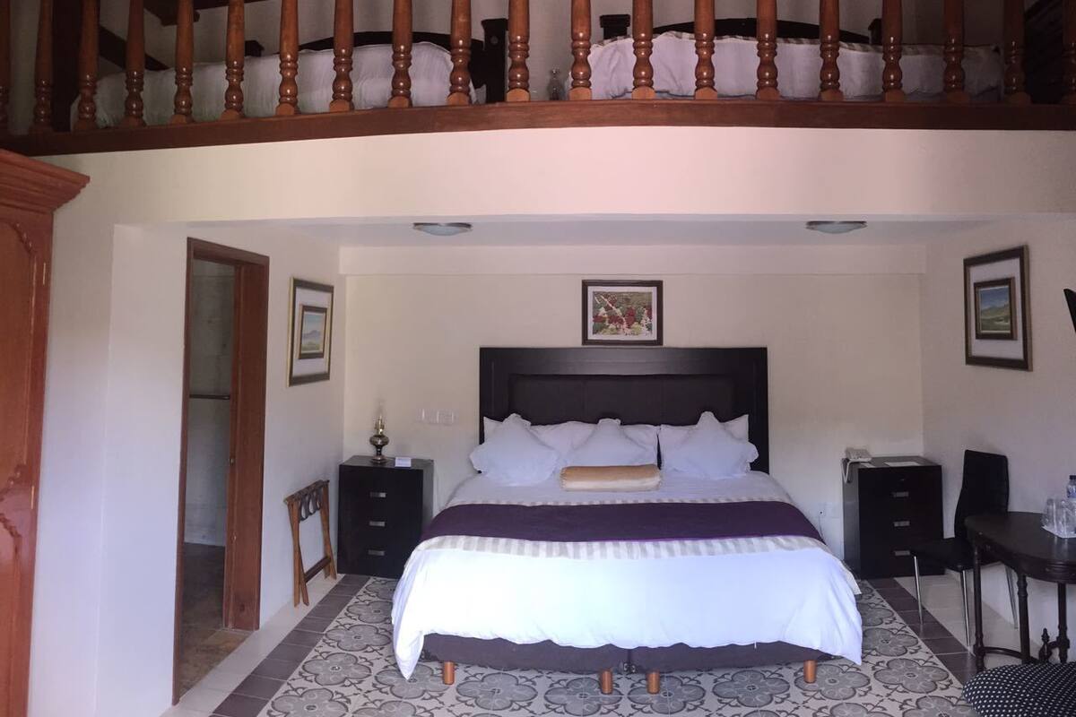 Quarto com uma cama grande, cabeceira de madeira, duas mesas de cabeceira, um criado-mudo e uma pequena mesa com cadeiras.