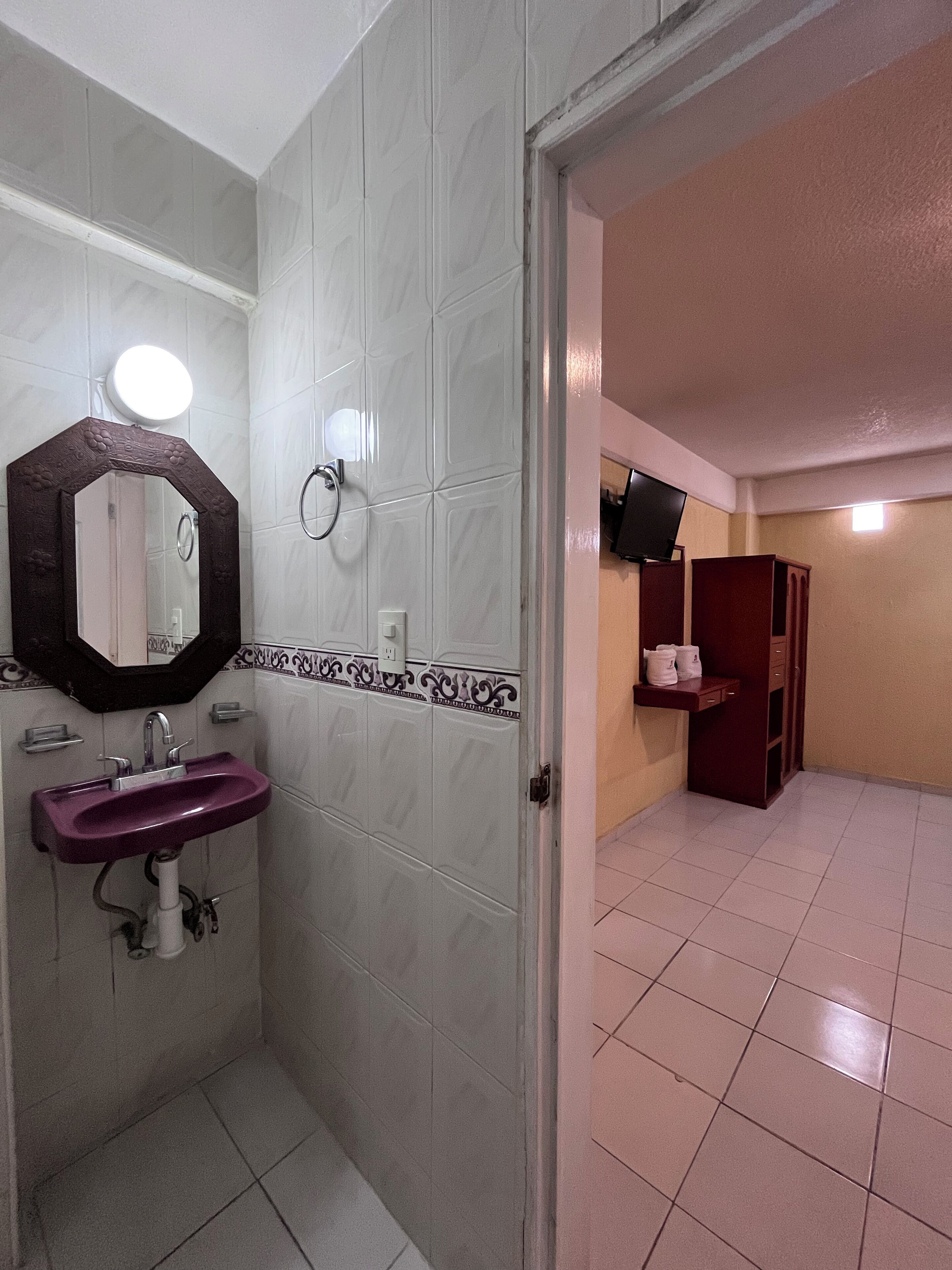 Casa de banho com lavatório roxo, espelho e sanita.