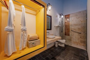 Uma casa de banho moderna com uma parede de destaque amarela, um espelho grande, cabine de duche em vidro e uma sanita.