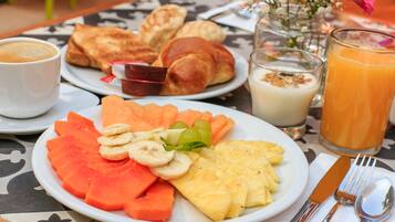 Uma mesa posta para o café da manhã, com pratos de frutas, doces e bebidas.