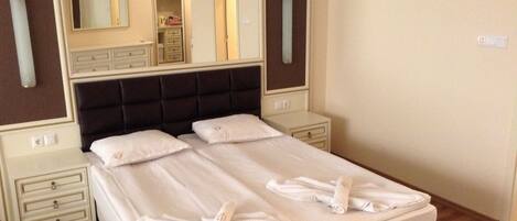 Quarto de hotel com uma cama grande, duas mesas de cabeceira, um guarda-roupa e um espelho.