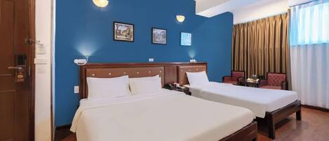 Quarto de hotel com duas camas, cabeceira de madeira, escrivaninha com cadeira e janela com cortinas.