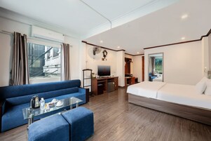Quarto de hotel com sofá, cama, televisão, mesa pequena e vista para o exterior.