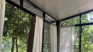 Piscina com água cristalina, rodeada por grandes janelas com cortinas brancas, e árvores visíveis lá fora.
