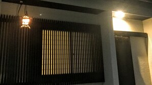 Um edifício com telhado inclinado, janela com persianas verticais e porta com uma pequena saliência.