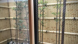 Quarto com cerca de bambu, janela e vista para um jardim com pedras e plantas.