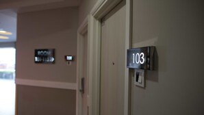 Um corredor com uma porta identificada com o número '103' e uma placa indicando 'QUARTO 103'.