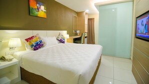 Quarto de hotel com cama, mesa de cabeceira com abajur, televisão, espelho e área de chuveiro.
