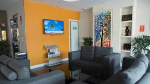 Uma sala de estar com sofás cinzas, uma televisão na parede e um quadro colorido.