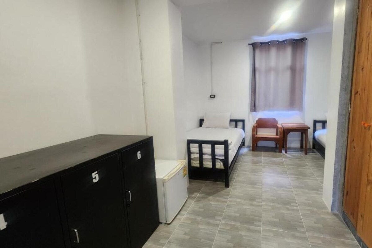 Quarto compacto com cama, uma pequena mesa, uma cadeira e um guarda-roupa.