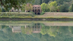 Um edifício histórico com estruturas em arco próximo a um lago tranquilo, rodeado por vegetação.