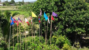 Um jardim com várias bandeiras, uma pequena árvore e uma área gramada.