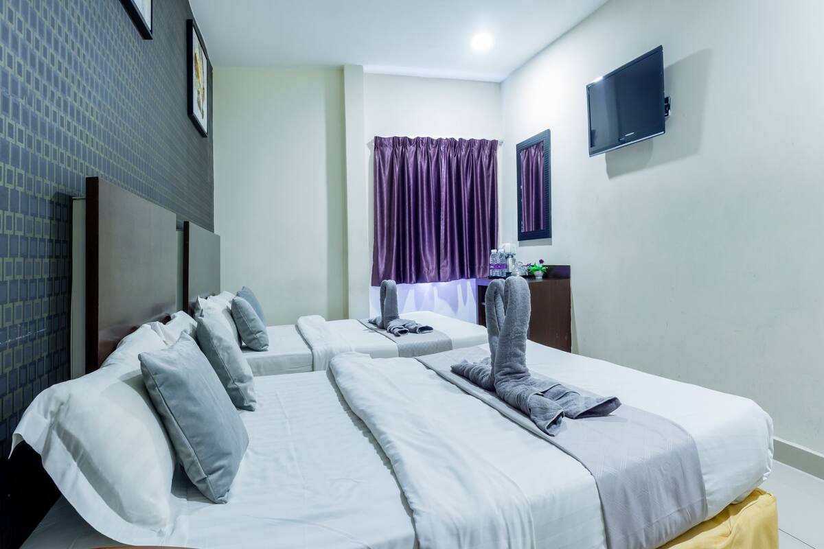 Quarto de hotel com duas camas, uma televisão, um espelho e uma janela com cortinas roxas.