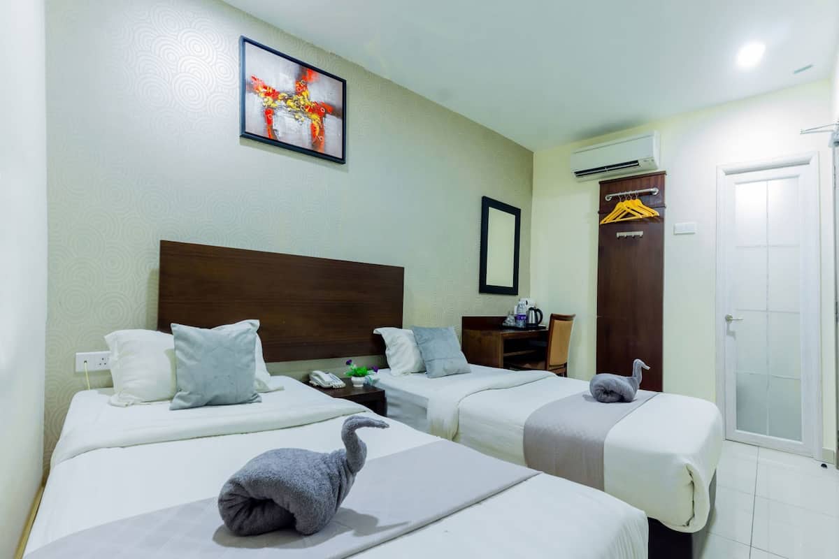 Quarto de hotel com três camas, cabeceira de madeira, um quadro na parede, uma mesa de trabalho com cadeira e um aparelho de ar condicionado.