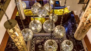 Luminárias pendentes ornamentadas com desenhos elaborados, um piso estampado e um vislumbre de um espaço com uma área iluminada em amarelo ao fundo.