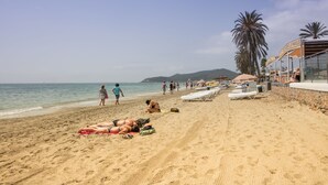 Uma praia com espreguiçadeiras, guarda-sóis e palmeiras.