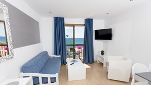 Uma sala de estar moderna com sofá, mesa de centro, TV e varanda com vista para o mar.