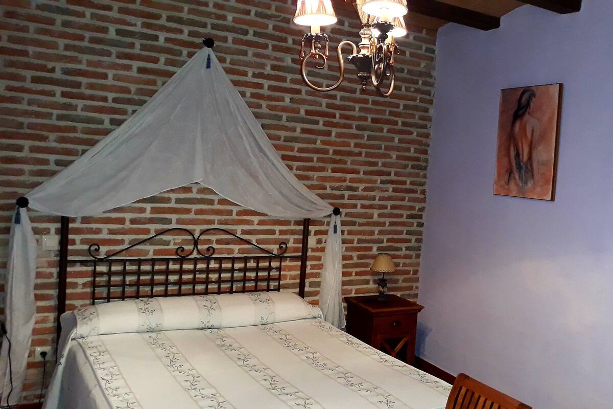 Quarto com cama de dossel, parede de tijolos e duas pinturas na parede.