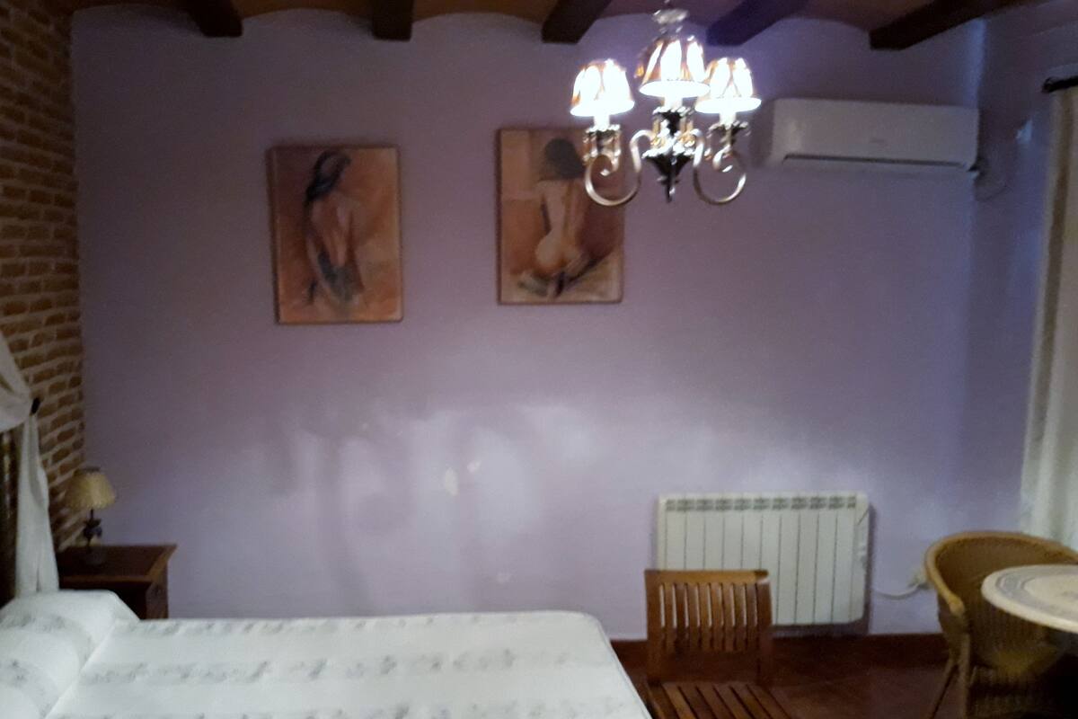 Quarto com cama, lustre, duas pinturas, radiador e uma cadeira.