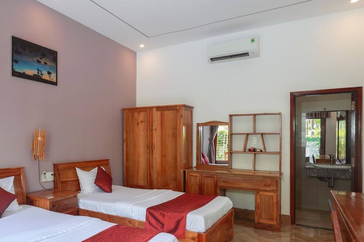 Quarto de hotel com duas camas, mobiliário de madeira, uma escrivaninha e um espelho.