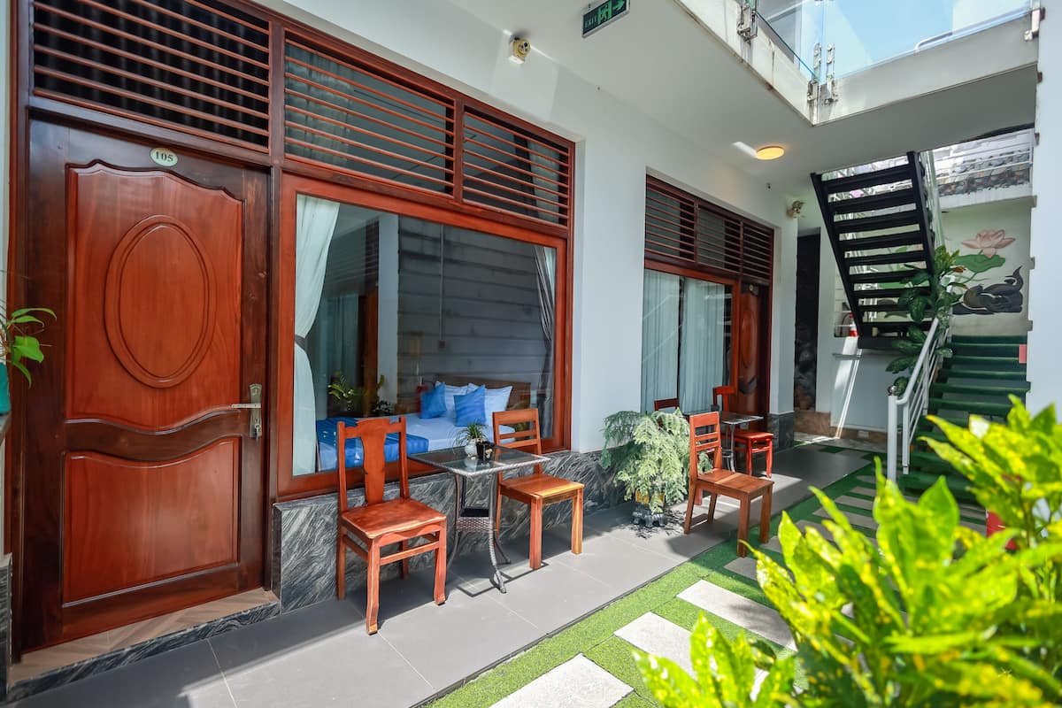Entrada de hotel com porta de madeira, área de estar com cadeiras e mesa, e escadaria.