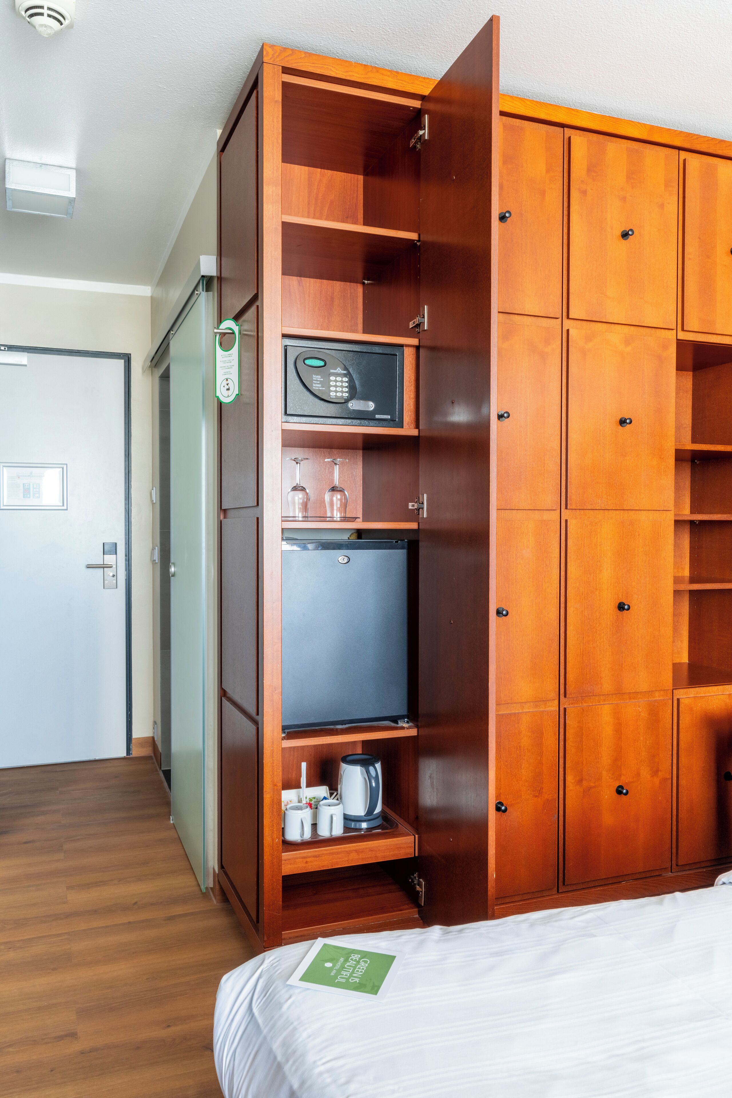 Quarto de hotel com guarda-roupa, cama, pequeno kitchenette e porta com placa.