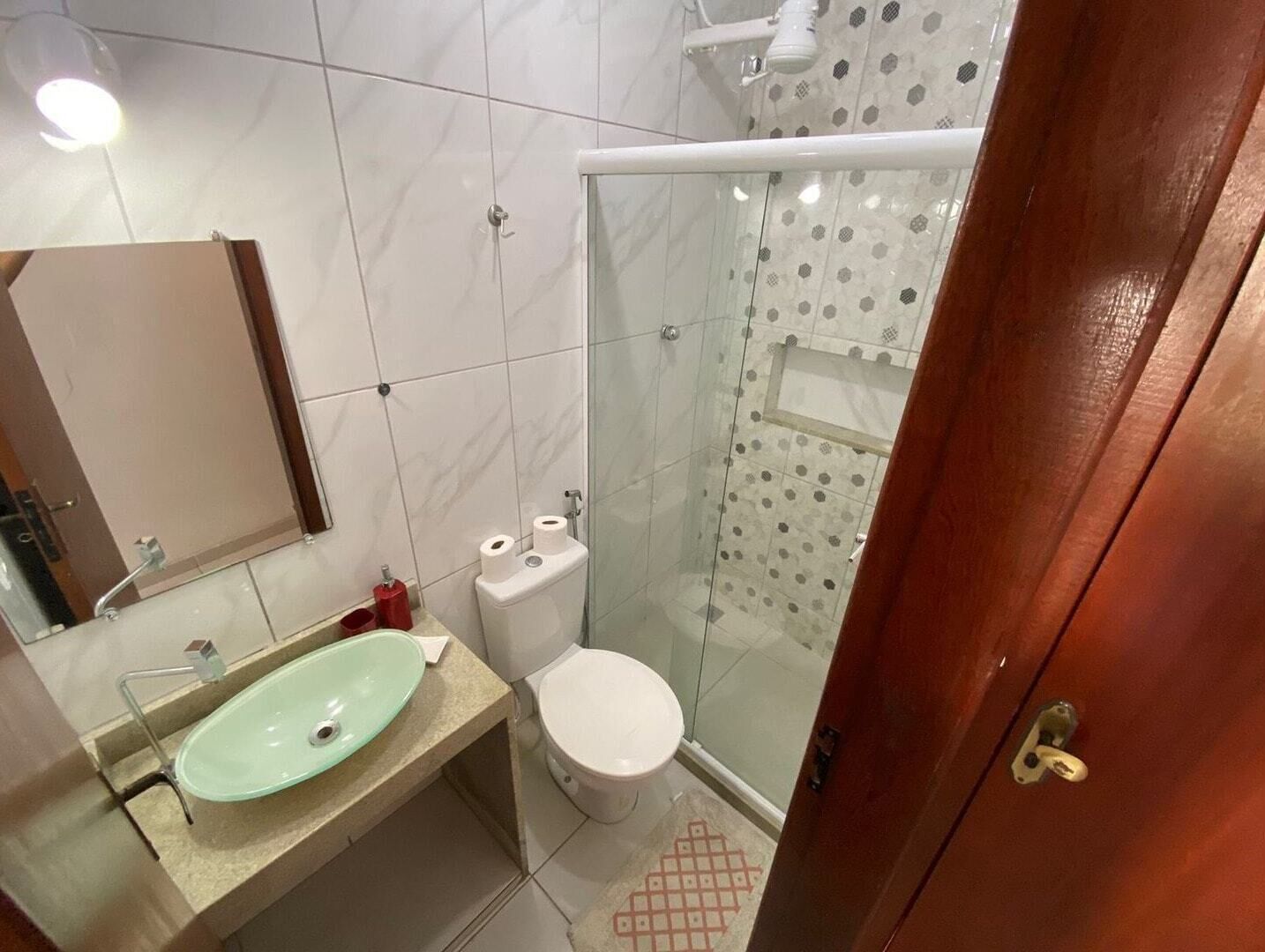 Casa de banho com cabine de chuveiro em vidro, sanita e lavatório com cuba de vidro.
